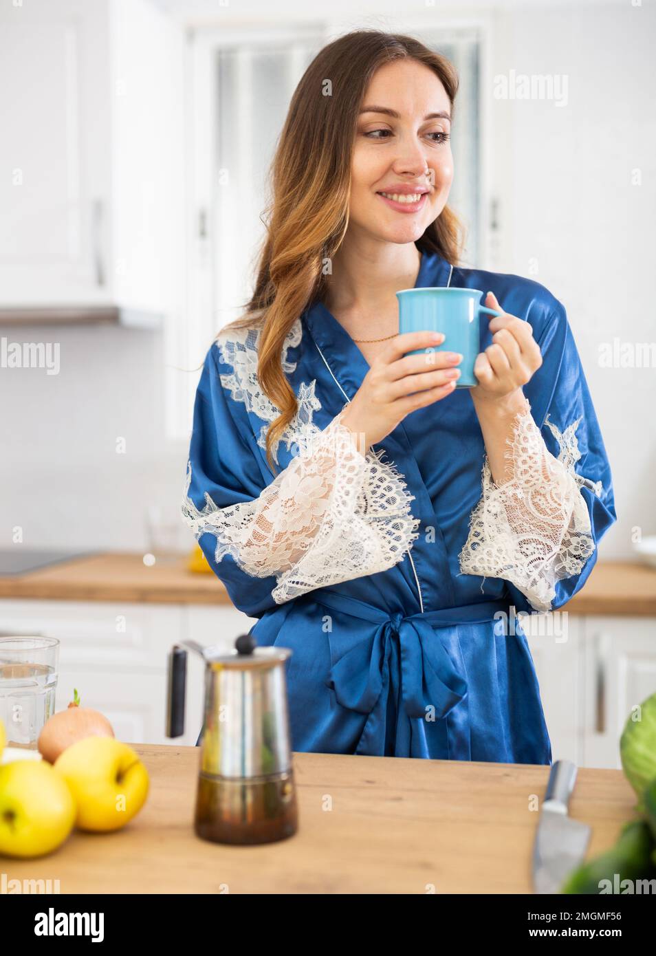 Young woman in blue dressing gown enjoying morning coffee in kitchen ...