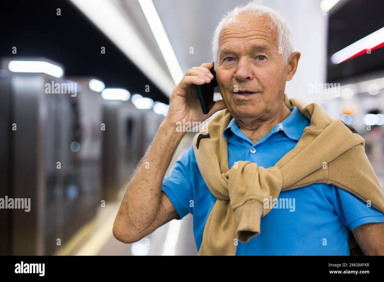 Elderly man using mobile phone while waiting for train in platform of ...