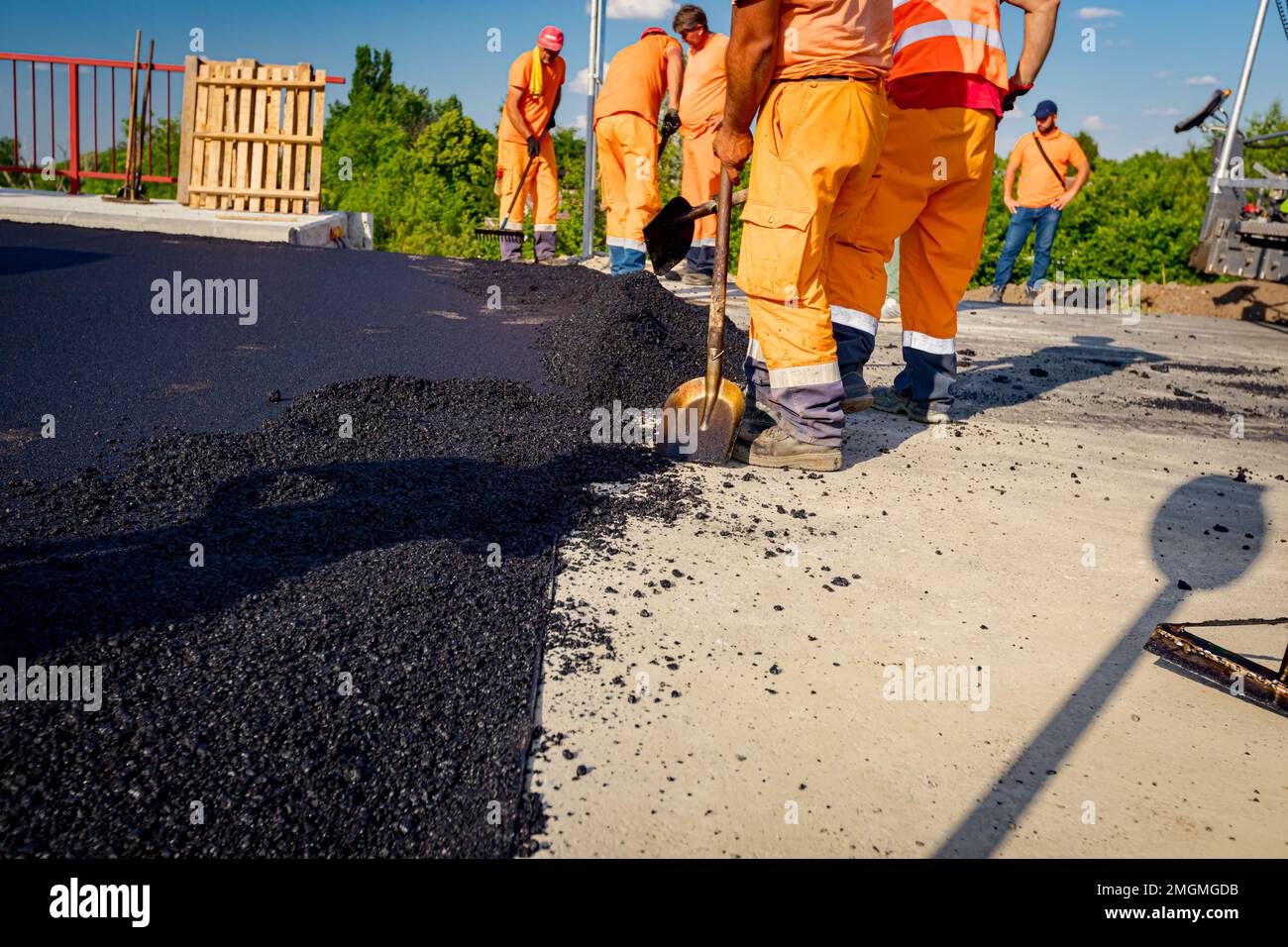 Few workers are using shovels to level, set up layer of fresh tarmac to ...