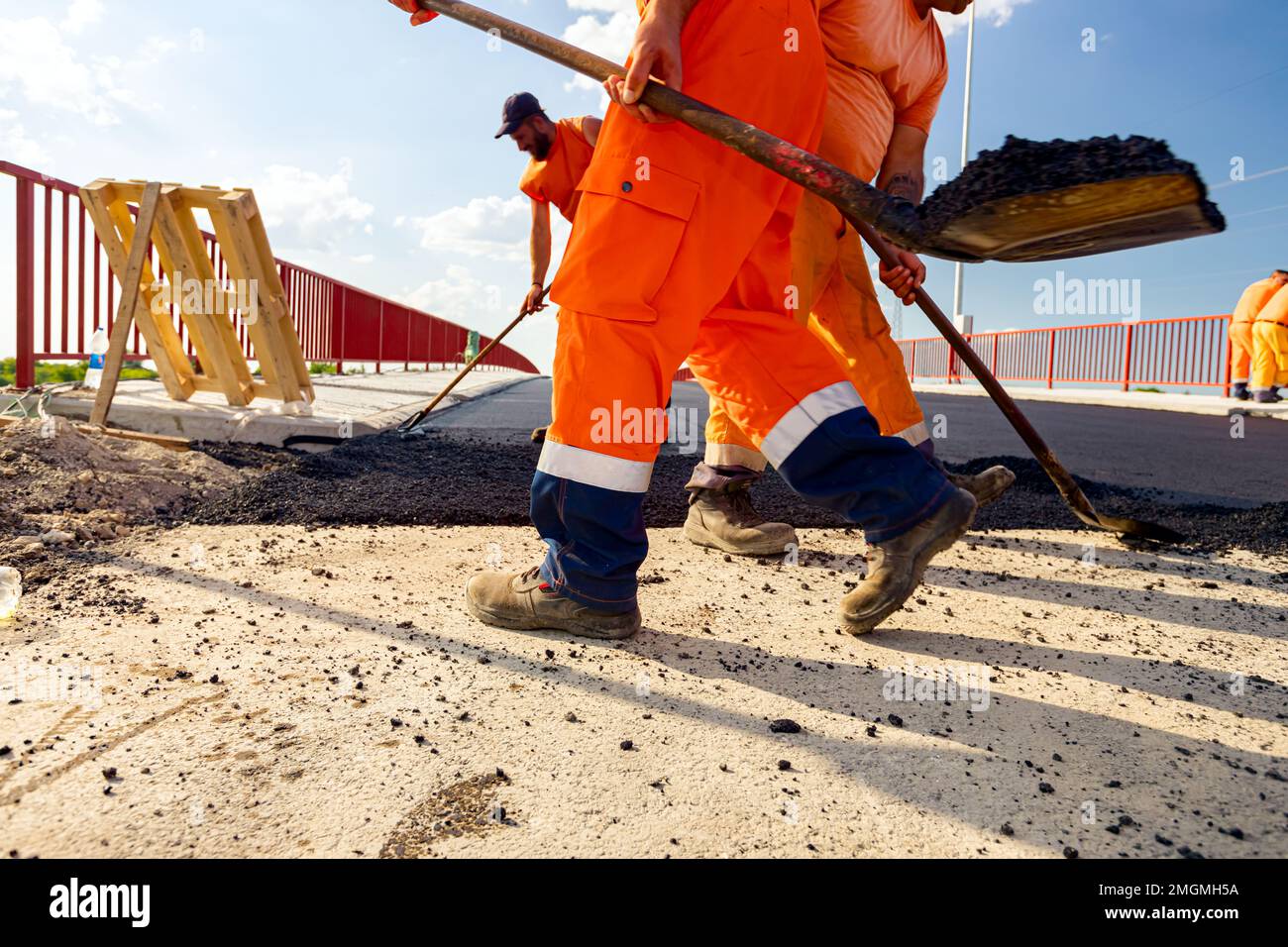 Few workers are using shovels to level, set up layer of fresh tarmac to ...