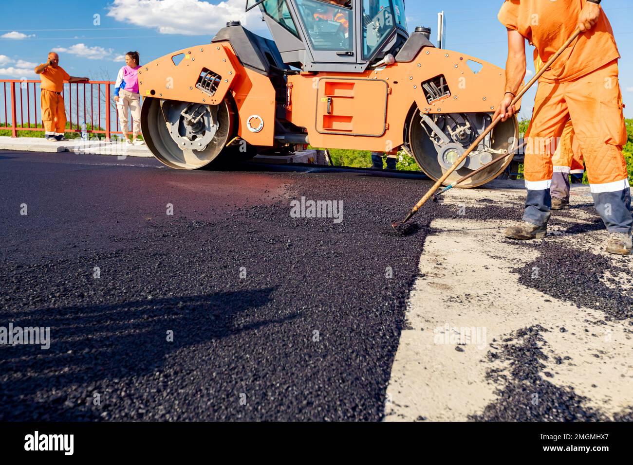 Workers are using rakes to level, set up layer of fresh tarmac to right ...