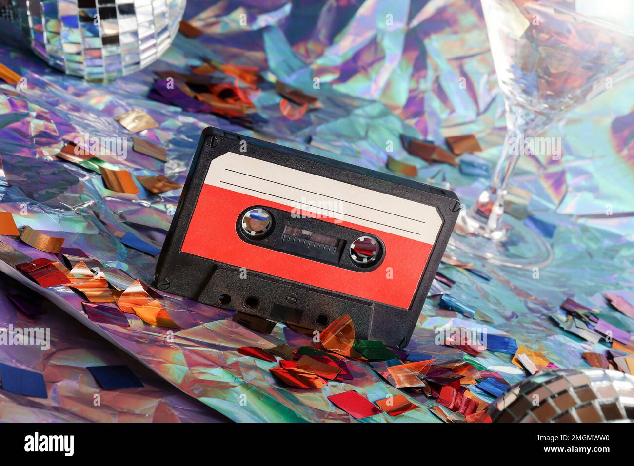 old cassette tape, disco ball and cocktail glass on crumpled neon ...