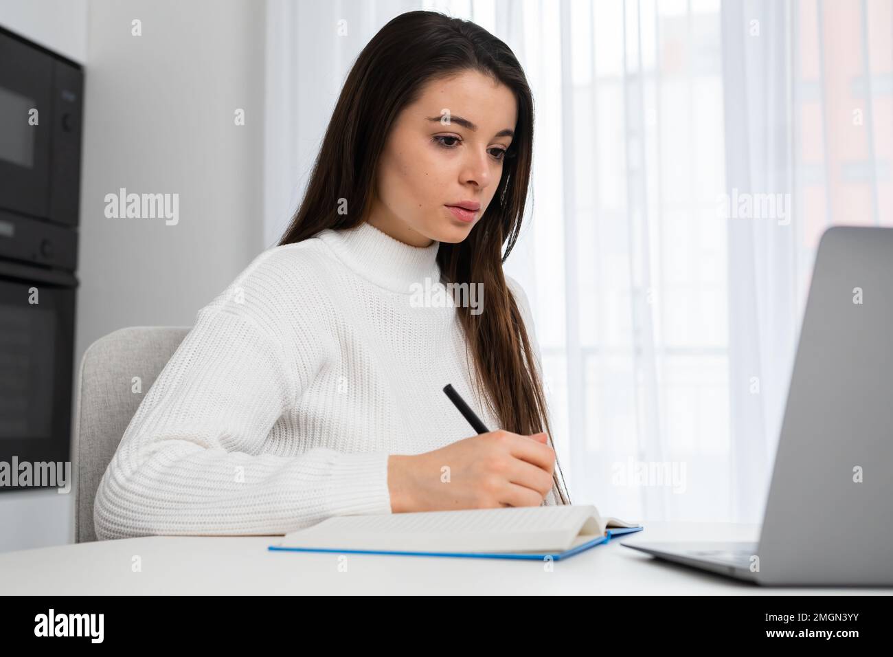 Portrait of a pensive young student making notes to the textbook during ...
