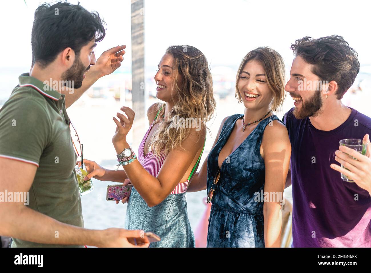 Four Caucasian friends enjoy a summer day at the beach by dancing in ...
