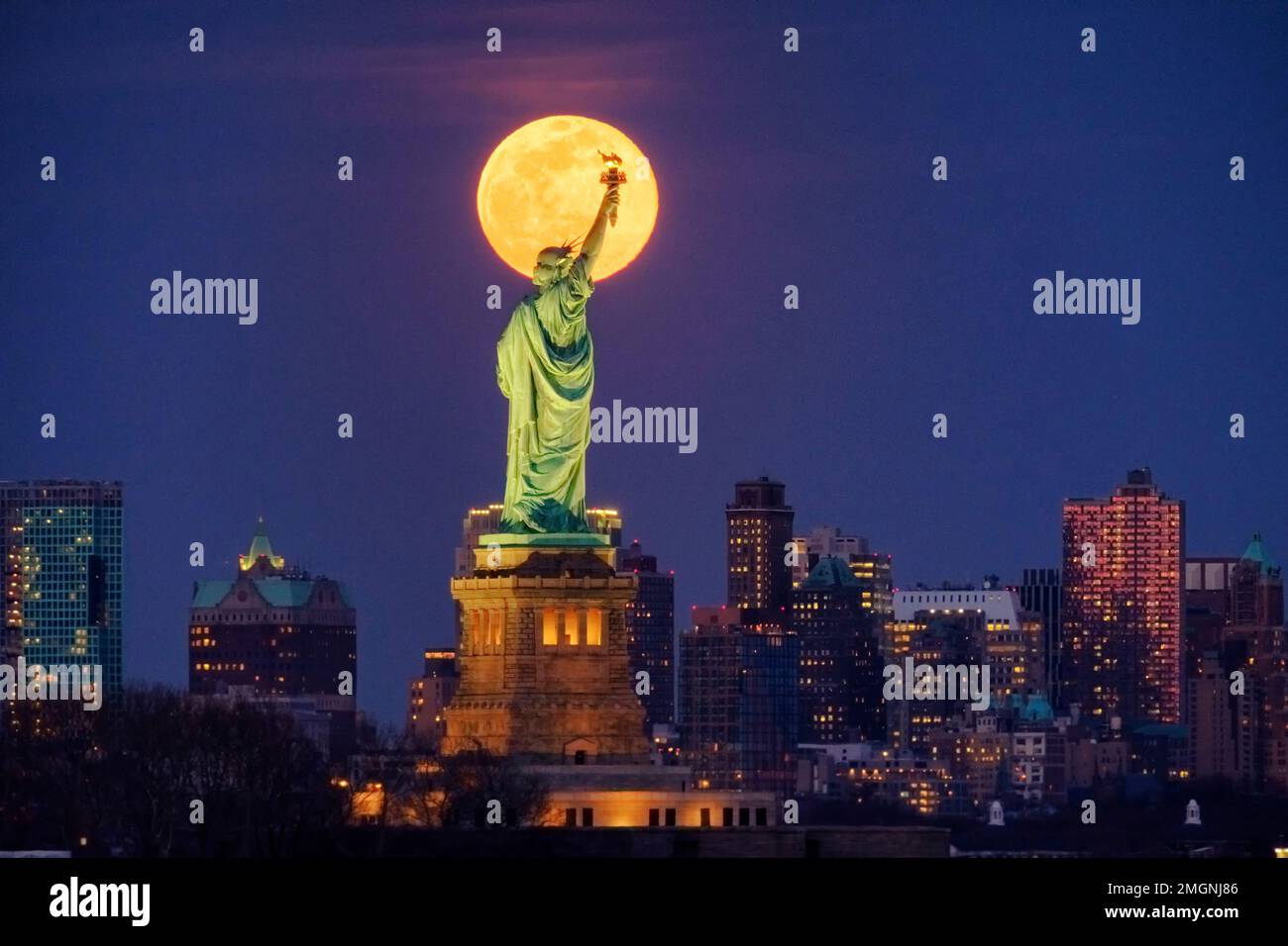 The rising full moon shines behind the Statue of Liberty, Monday ...