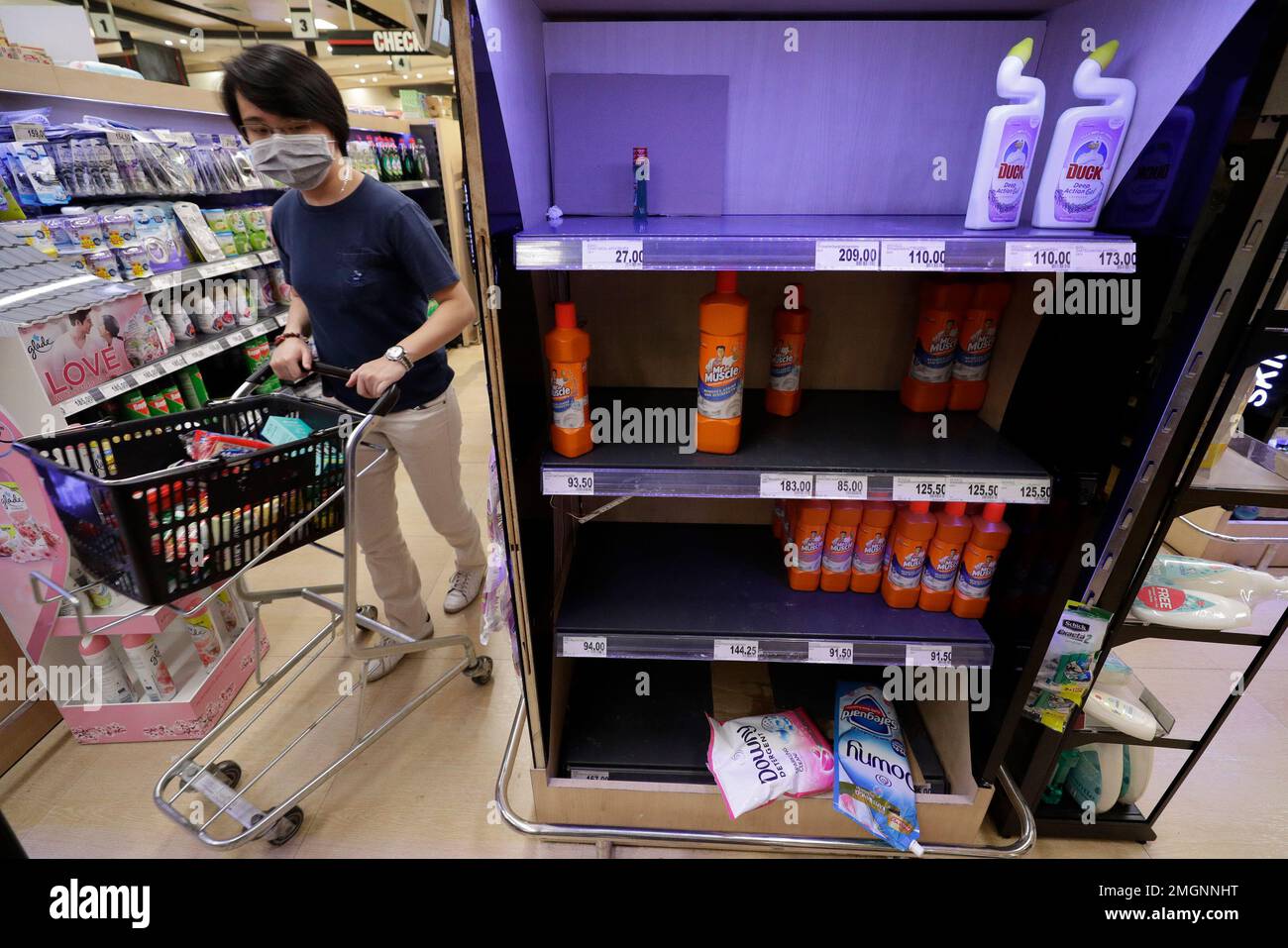 A woman wearing a protective mask walks past shelves which contain ...