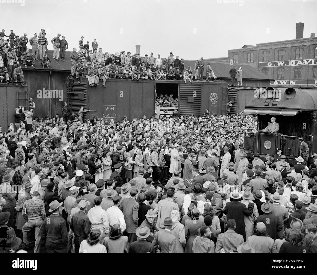 People crowd around the rear of the train and on box cars to hear ...