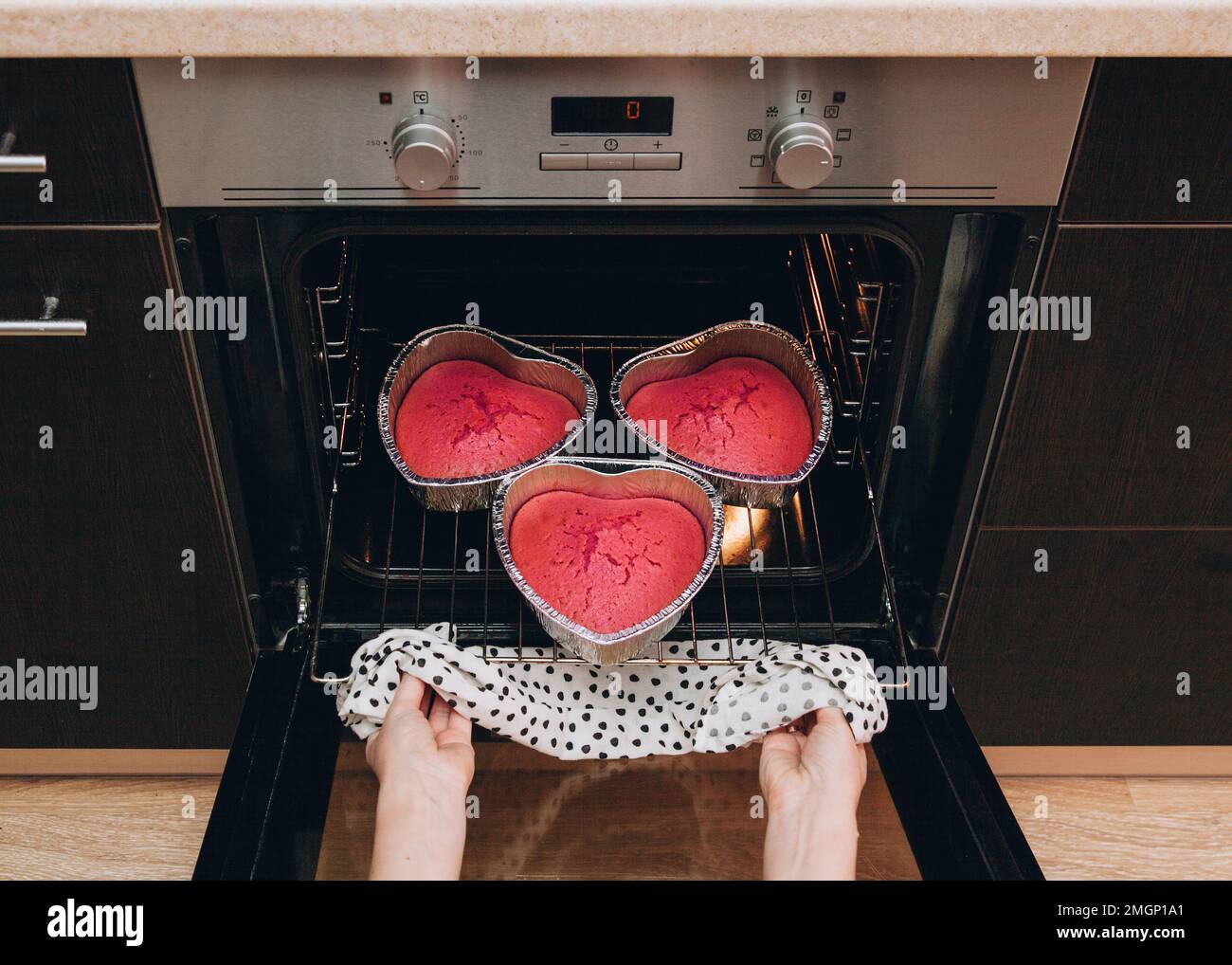 A woman takes out of the oven sponge cakes for a heart-shaped cake for ...