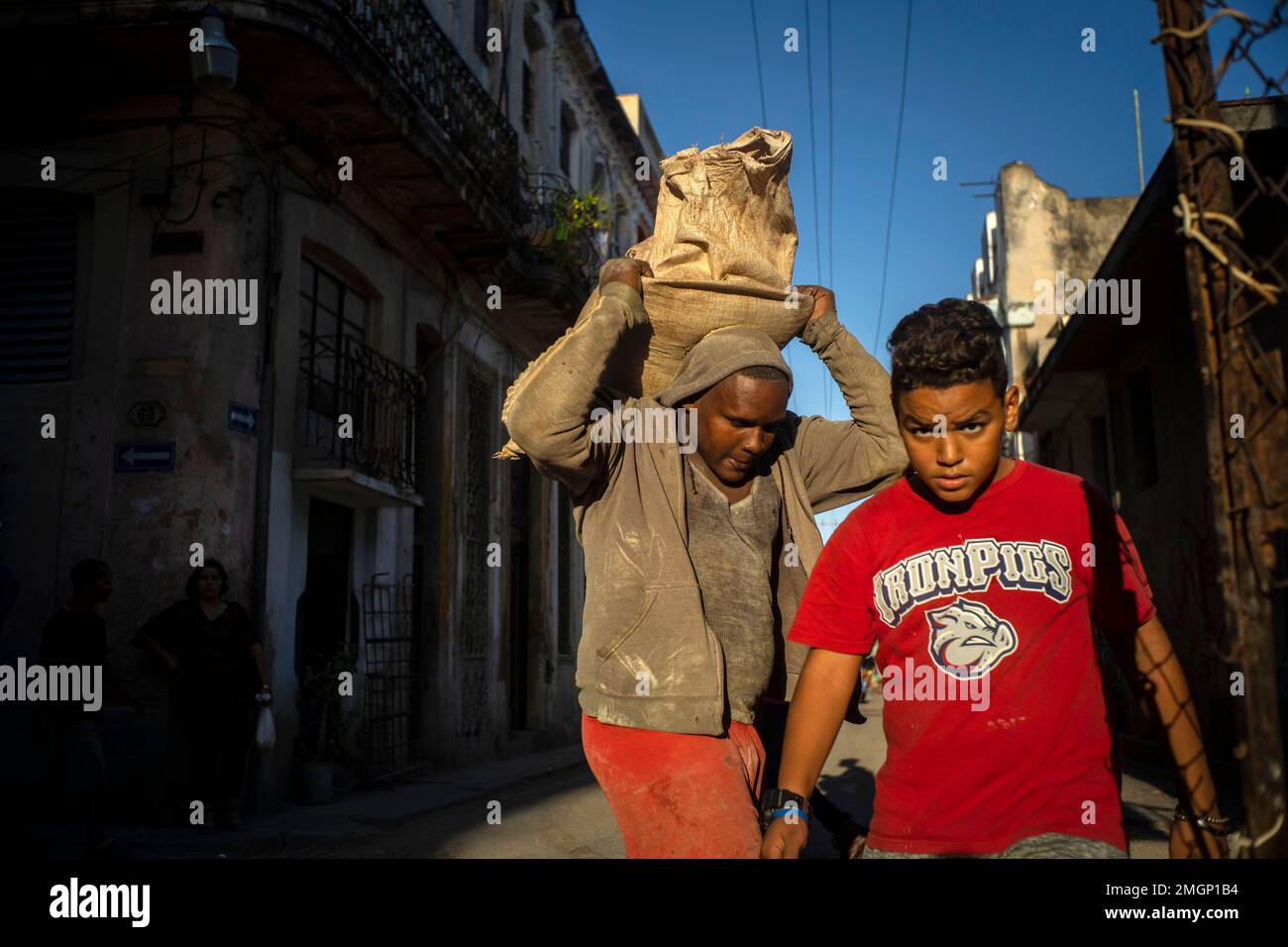 A construction worker carries a heavy bag of sand on his shoulders as a ...