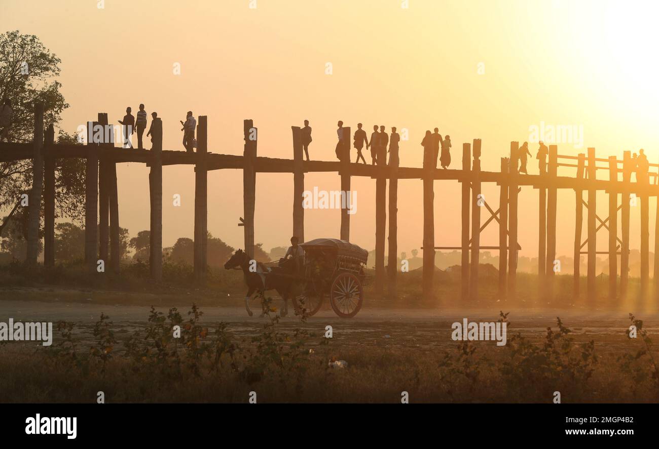 A horse and cart pass as visitors walk along the U Bein Bridge, a long ...