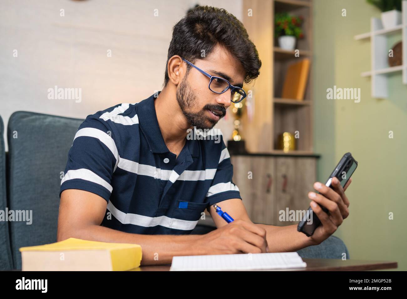 Young man using mobile phone for writing notes at home while listening ...