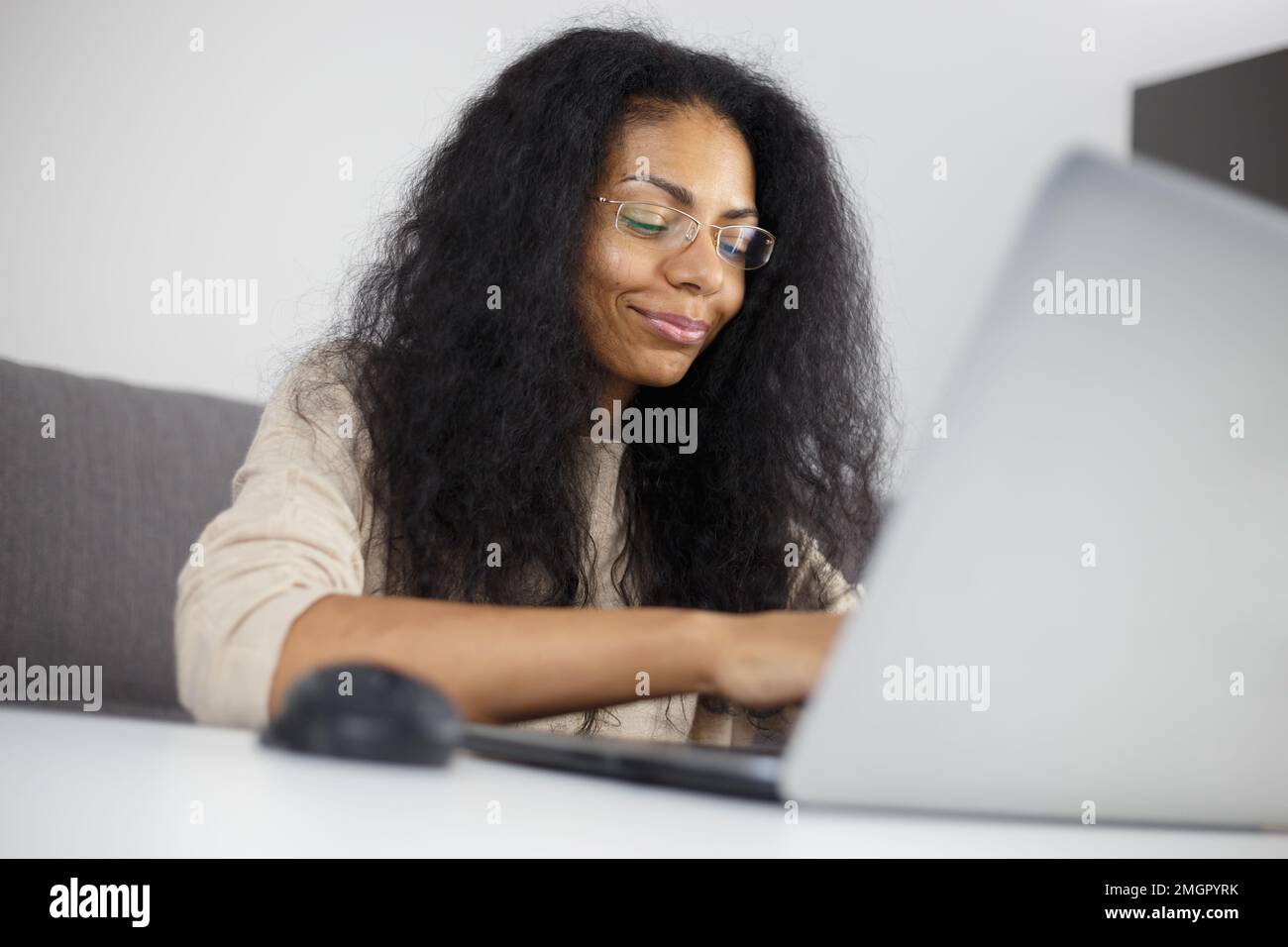 Cheerful black woman typing text on notebook keyboard at home. POC ...