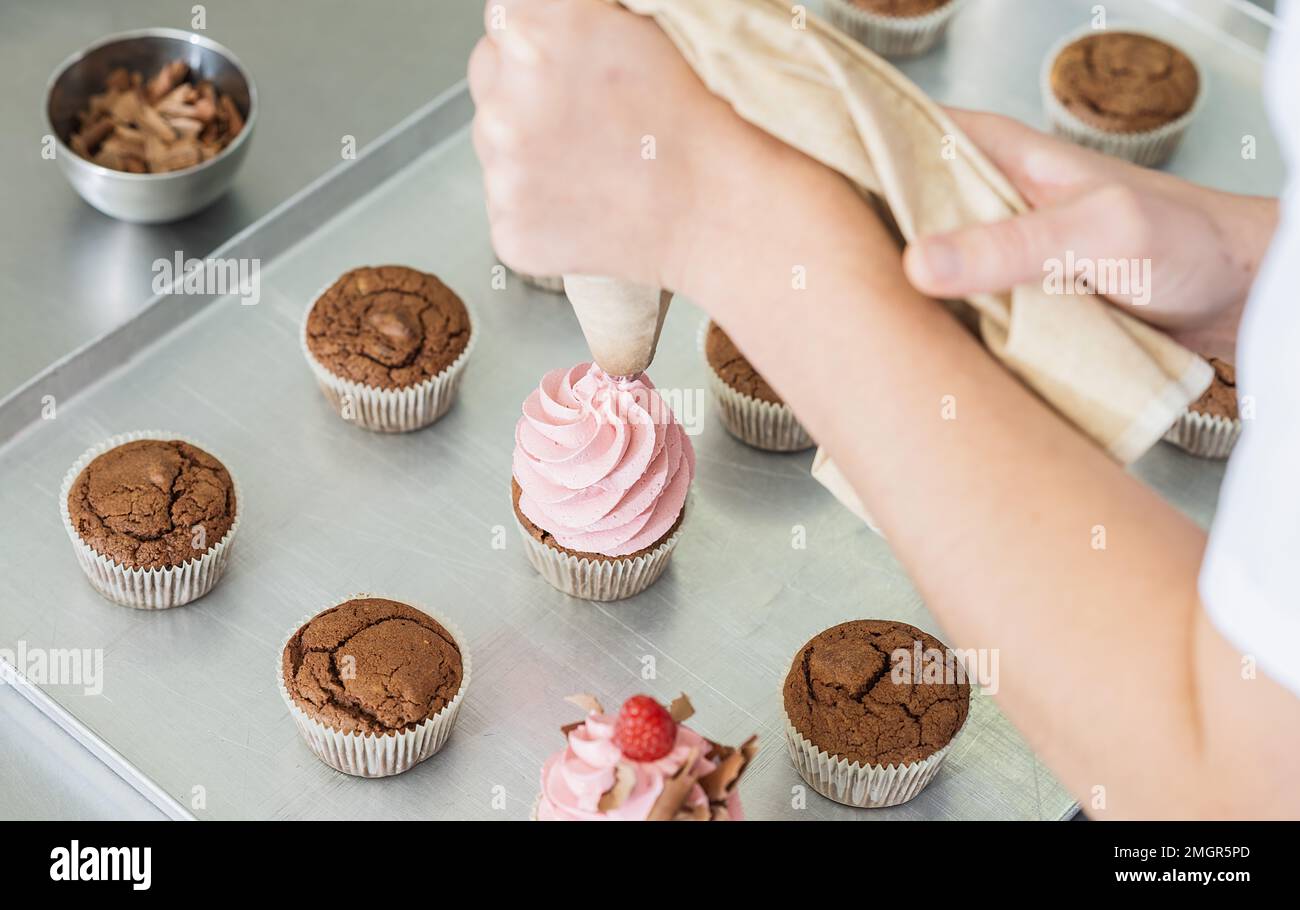 women in pastry bakery as confectioner glazing muffins with icing bag ...