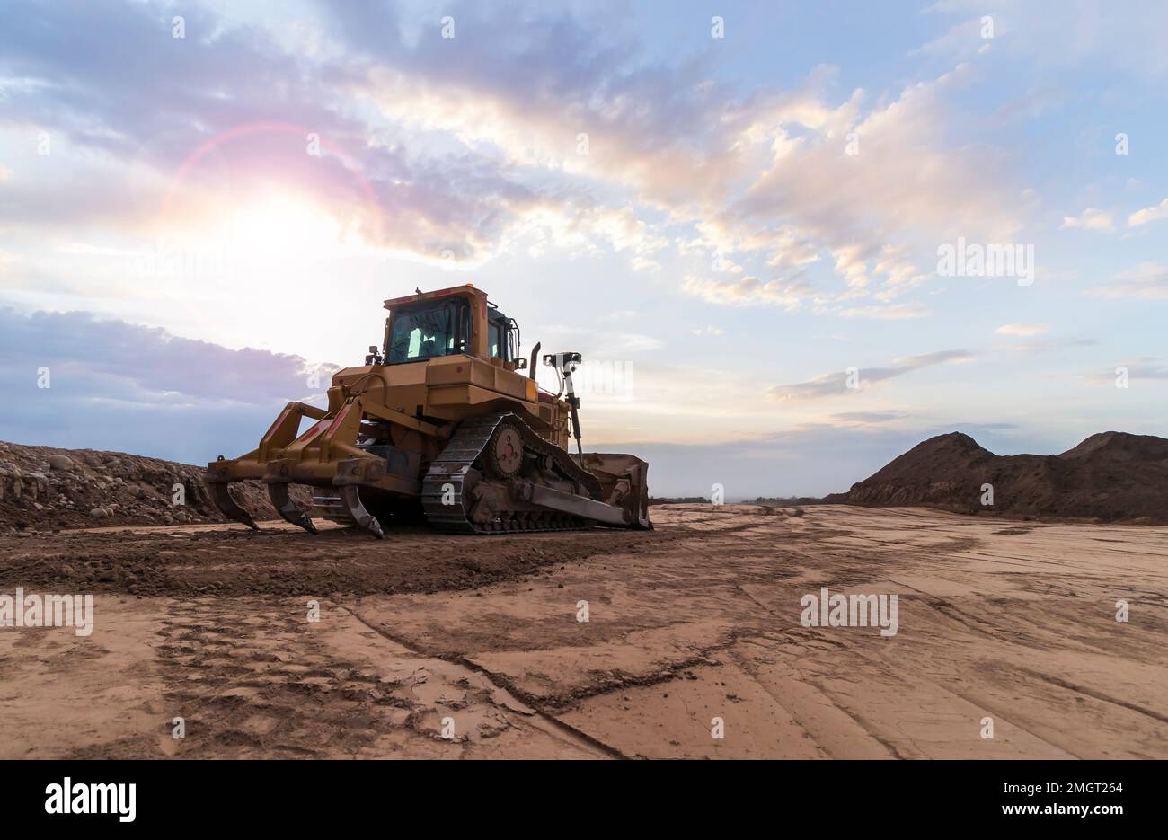 The yellow bulldozer stands on the ground. Against the background of ...