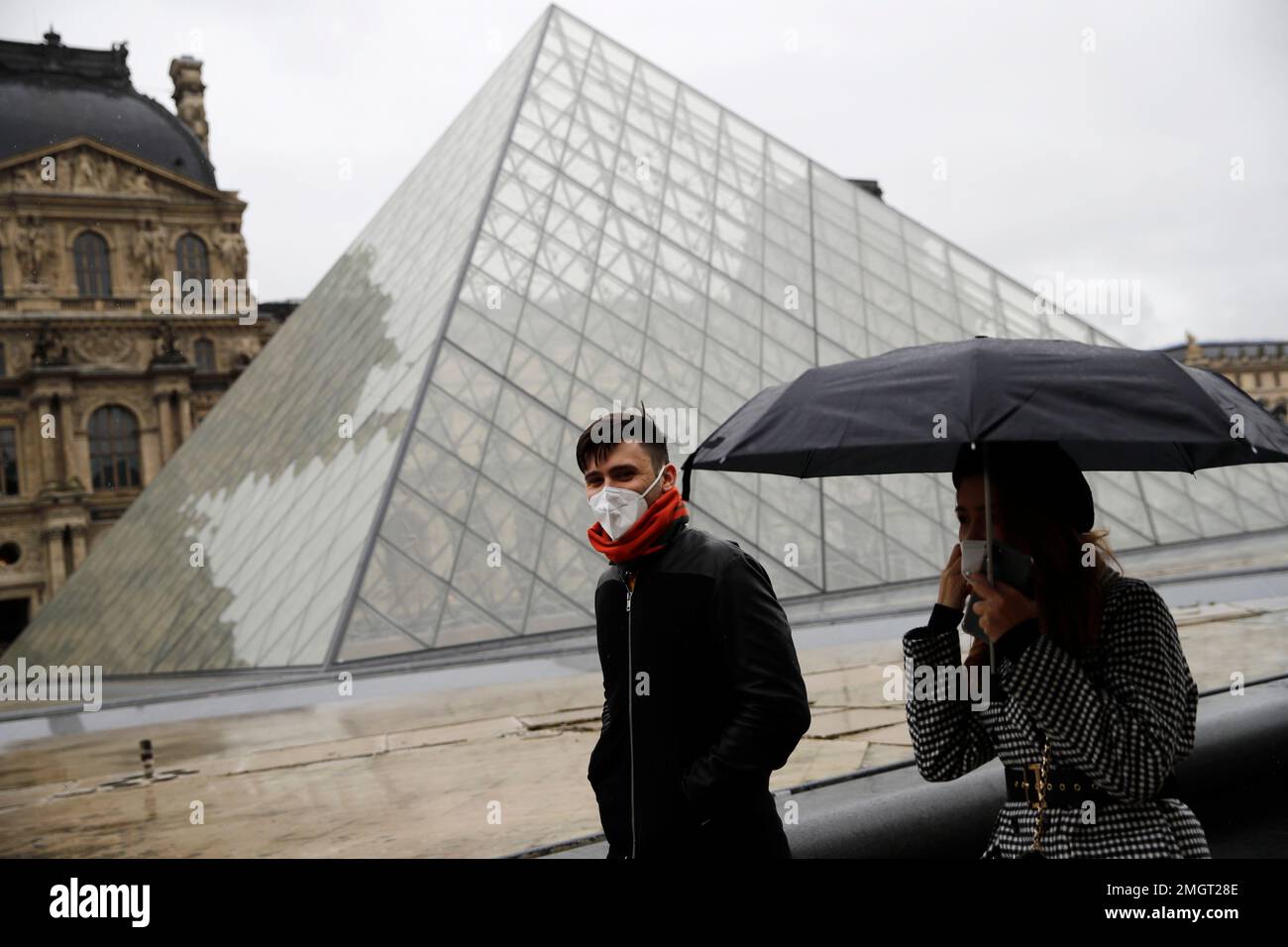 Tourists wearing a mask walks away from the Louvre museum in Paris ...