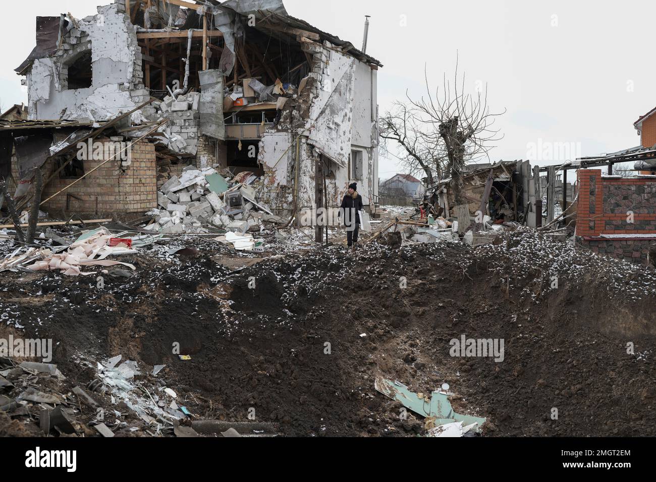 A woman stands on top of a crater next to a destroyed house after a ...