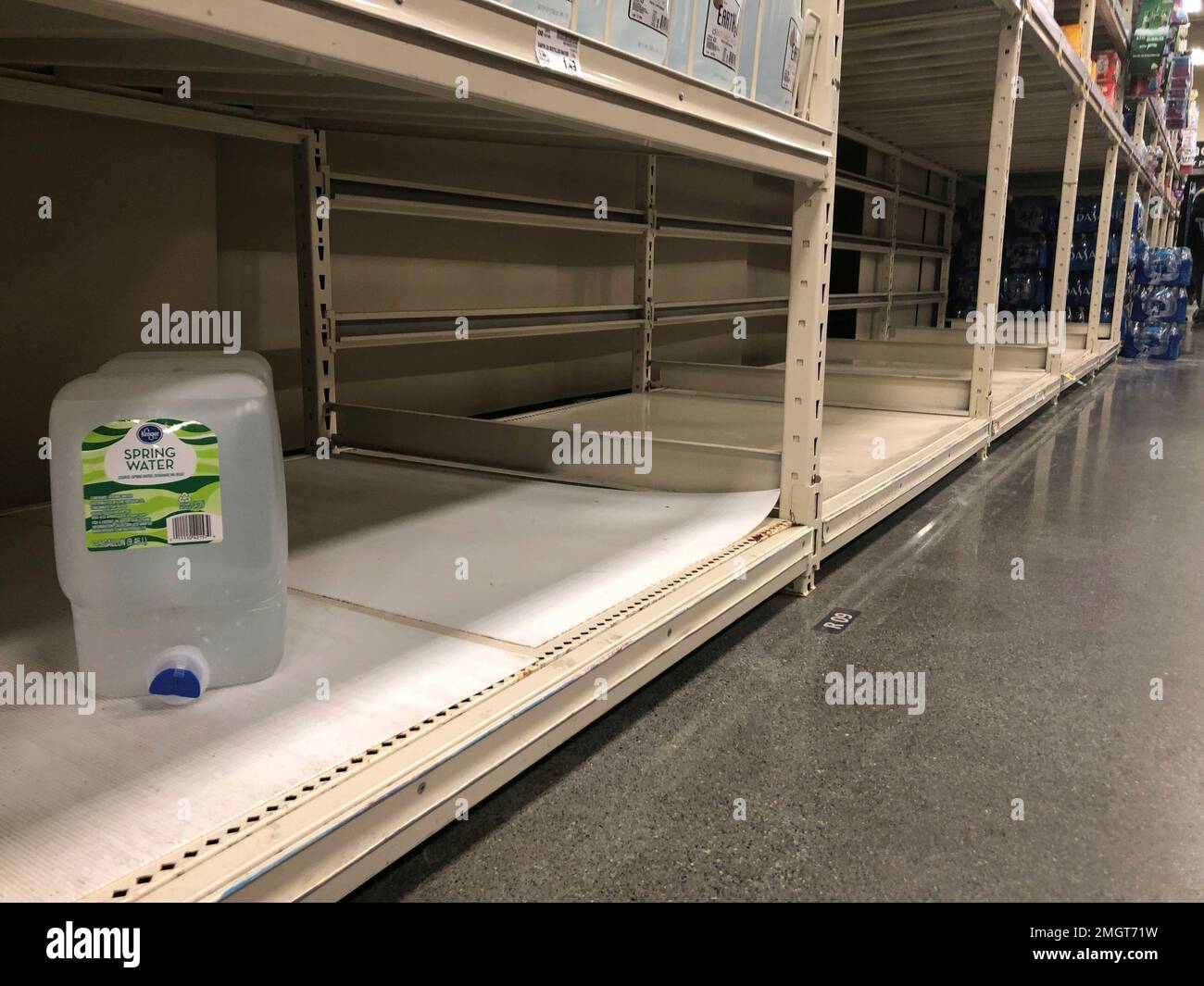 A lone container of water sits on otherwise empty shelving at a grocery ...