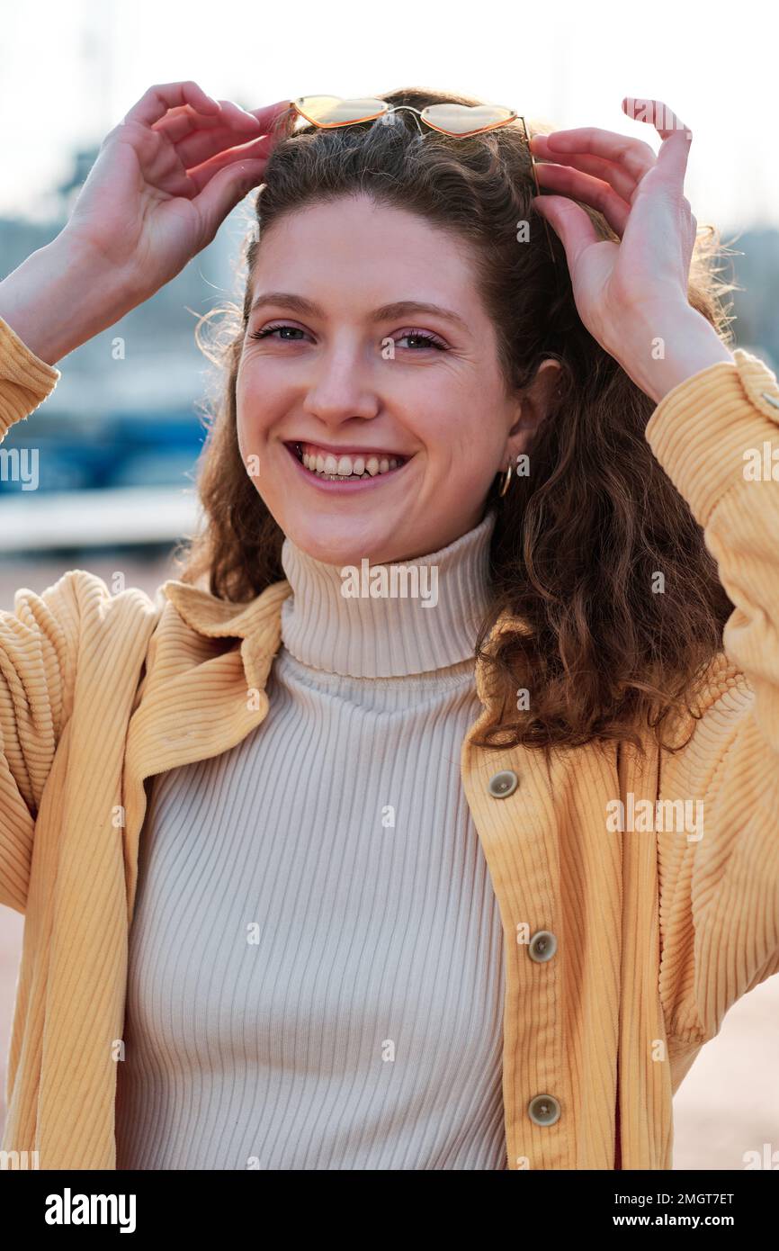 Woman looking at the camera and smiling while putting sunglasses on ...