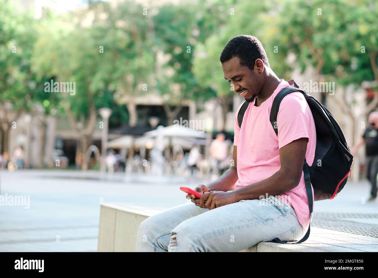 Man with backpack using a mobile phone while sitting on a bench ...