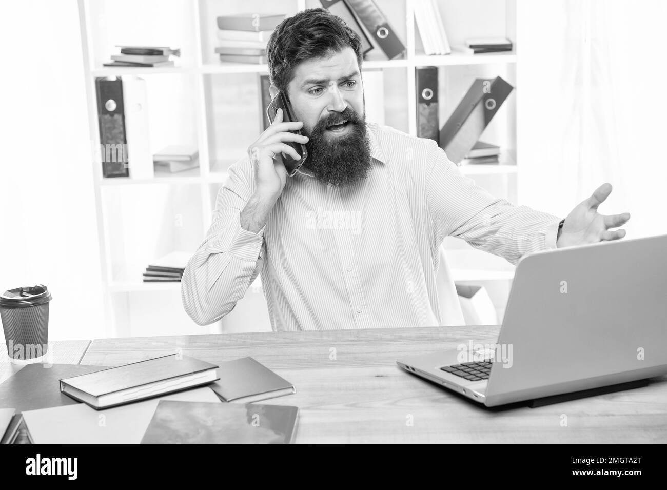 Stressed manager yelling on mobile phone working on laptop in office ...
