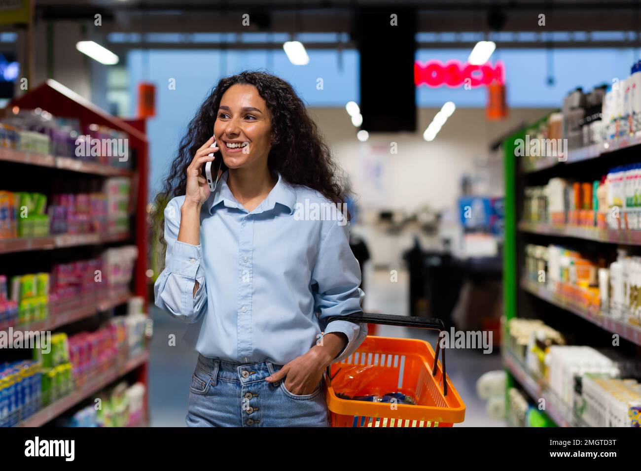 Smiling Hispanic woman shopper in supermarket, walks between rows of ...