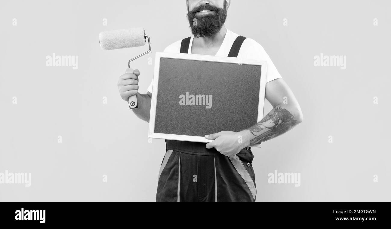 cropped man painter in work clothes hold paint roller and blackboard ...