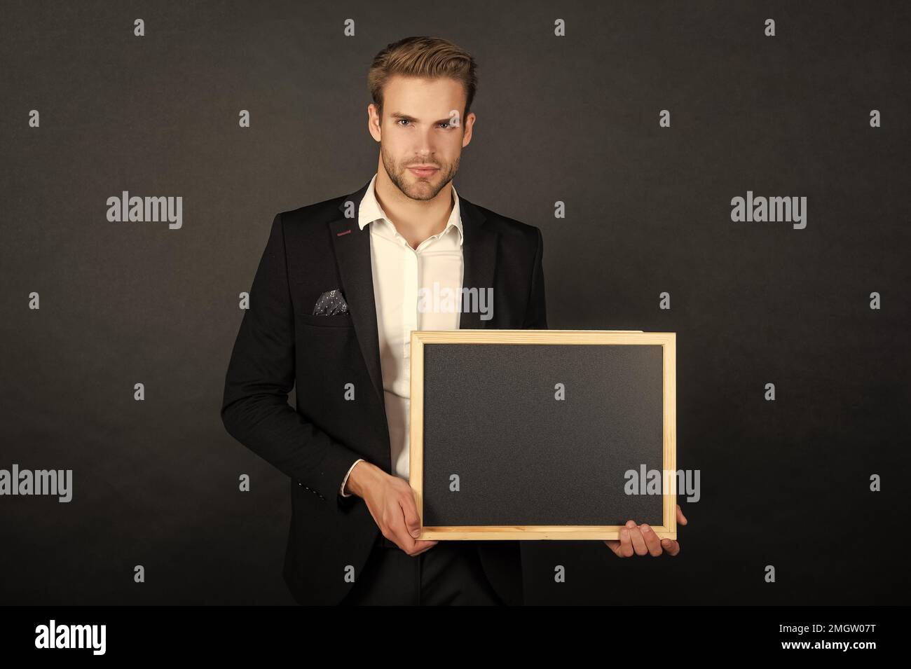 Serious guy in formal suit holding empty school blackboard copy space ...