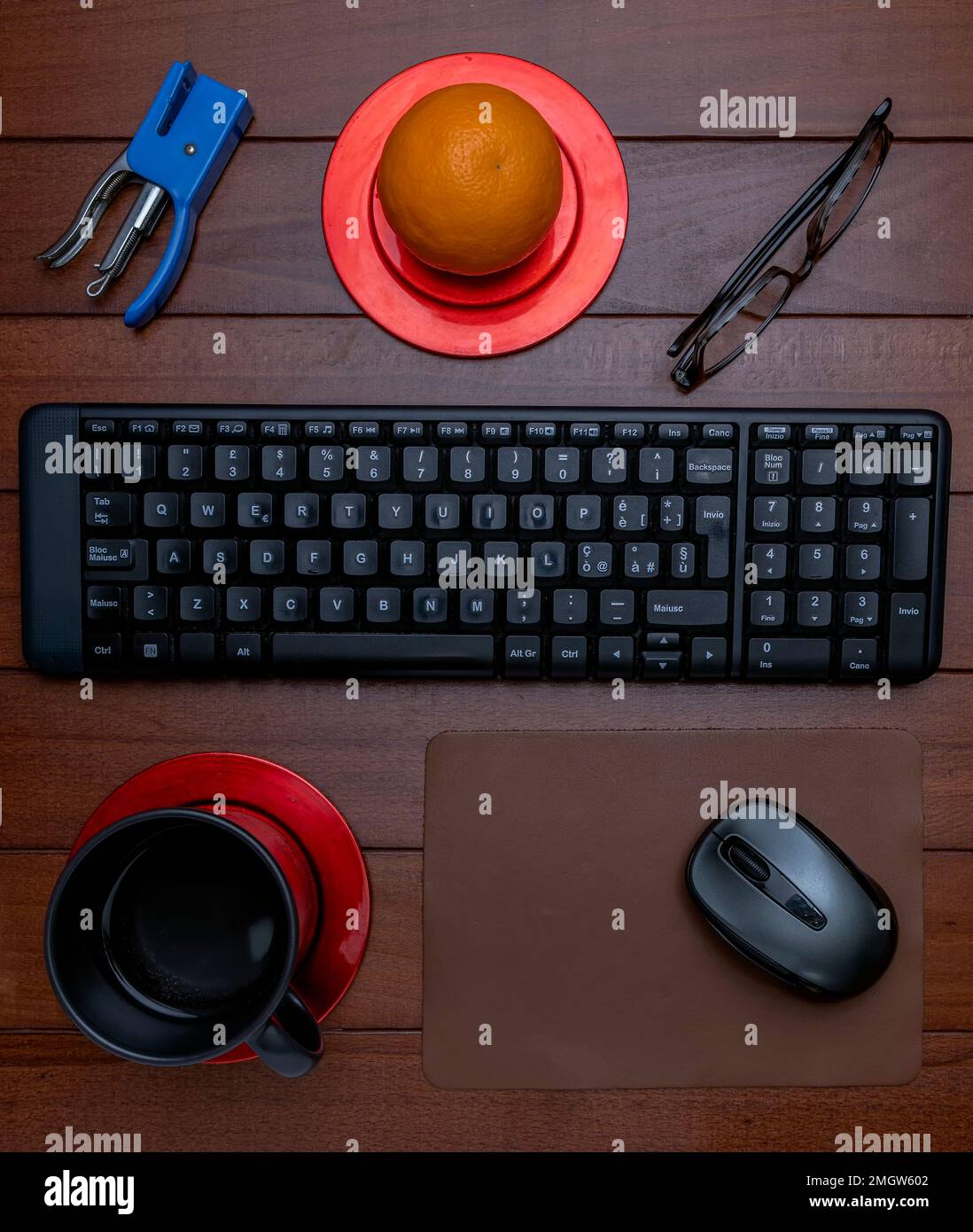 Composition of keyboard, mouse on pad, stapler, eyeglasses, an orange ...