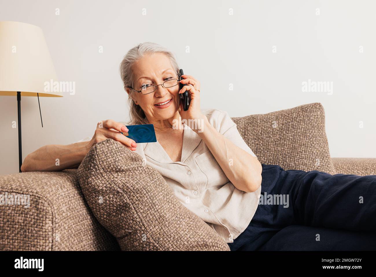 Aged woman making a call and holding a credit card. Senior female ...