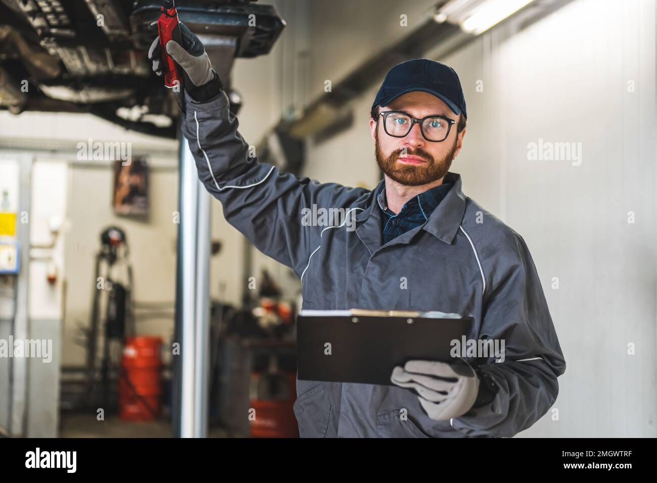 Mechanic inspecting car on lift using the checklist on a clipboard in a car repair shop. High ...