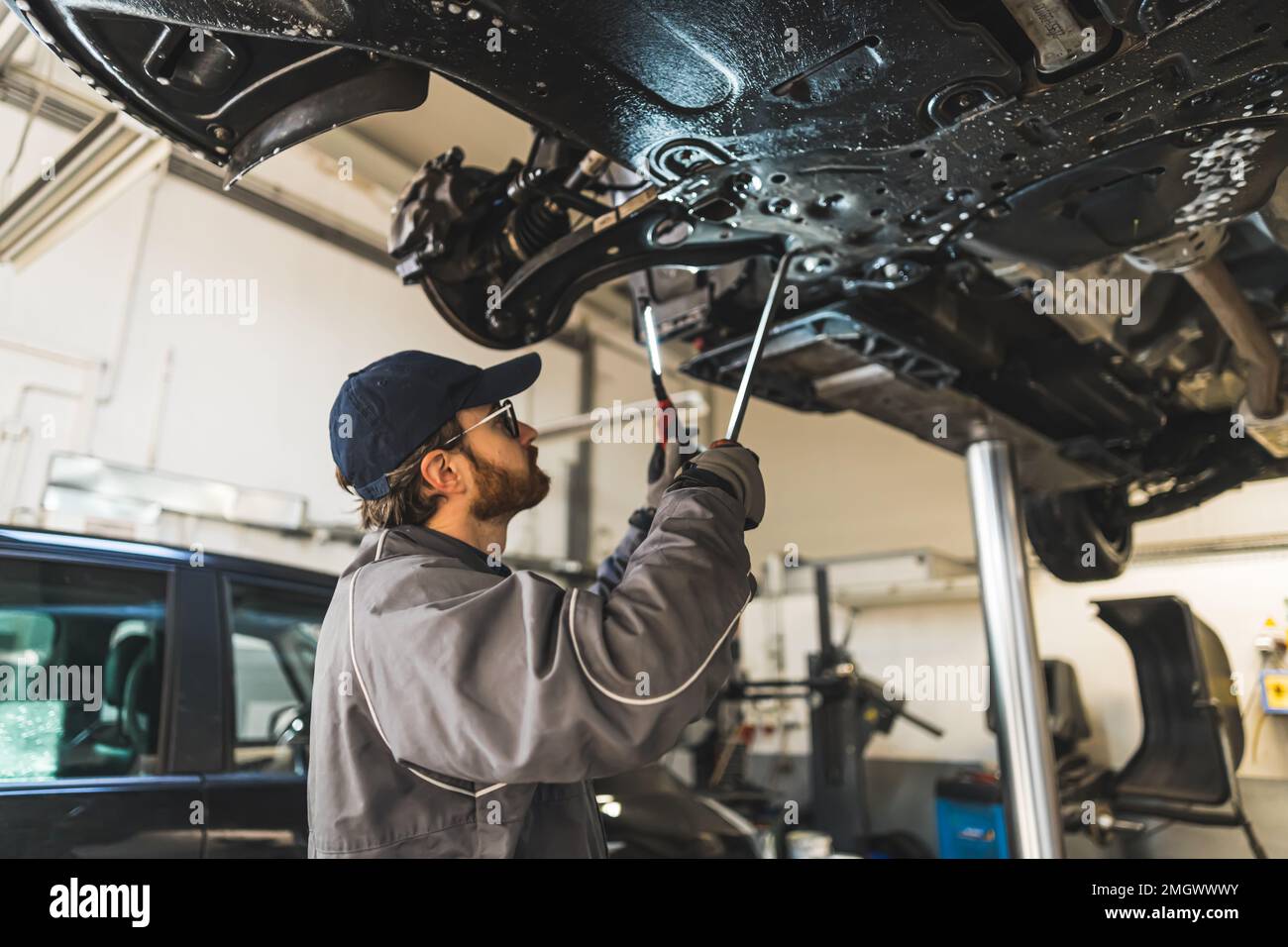 Skilled mechanic under a car on a lift using an LED light for chassis ...