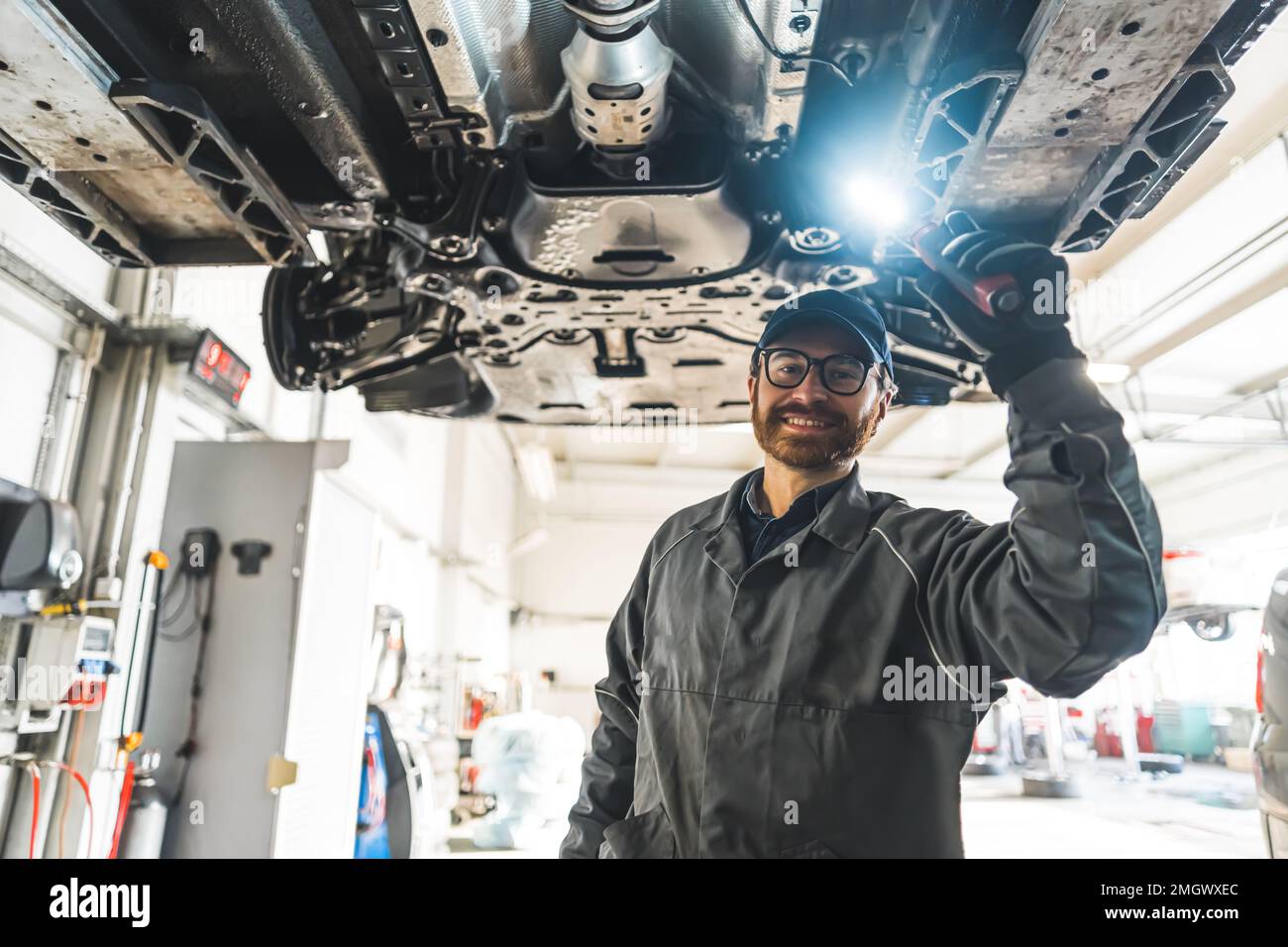 Skilled mechanic under a car on a lift using an LED lamp for chassis ...