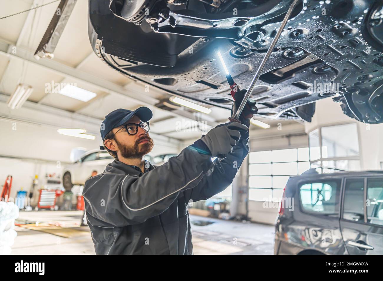 Skilled mechanic under a car on a lift using an LED lamp for chassis ...