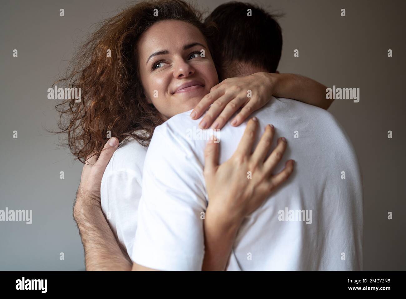 Young adult brunette curly hair woman wearing hugging her boyfriend against plain background and ...