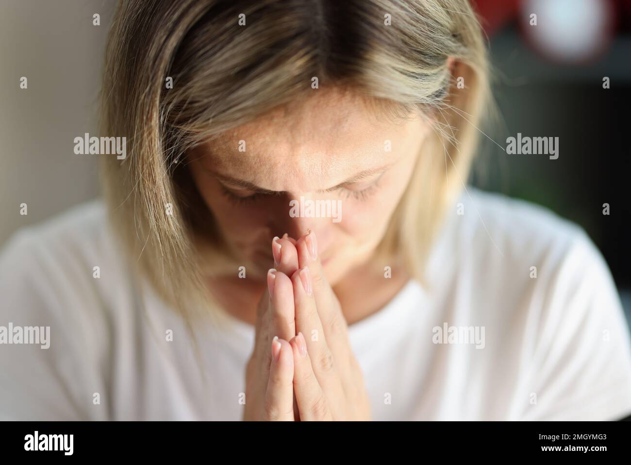 Woman with serious face holds her hands near her face as gesture of ...