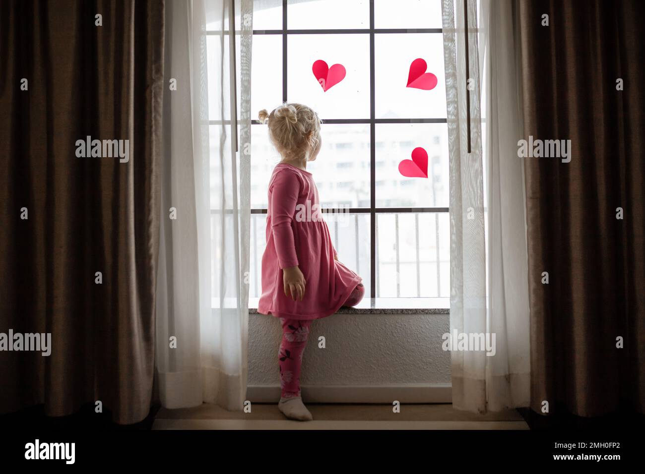 Young girl looking out window with hearts on Valentine's Day Stock ...