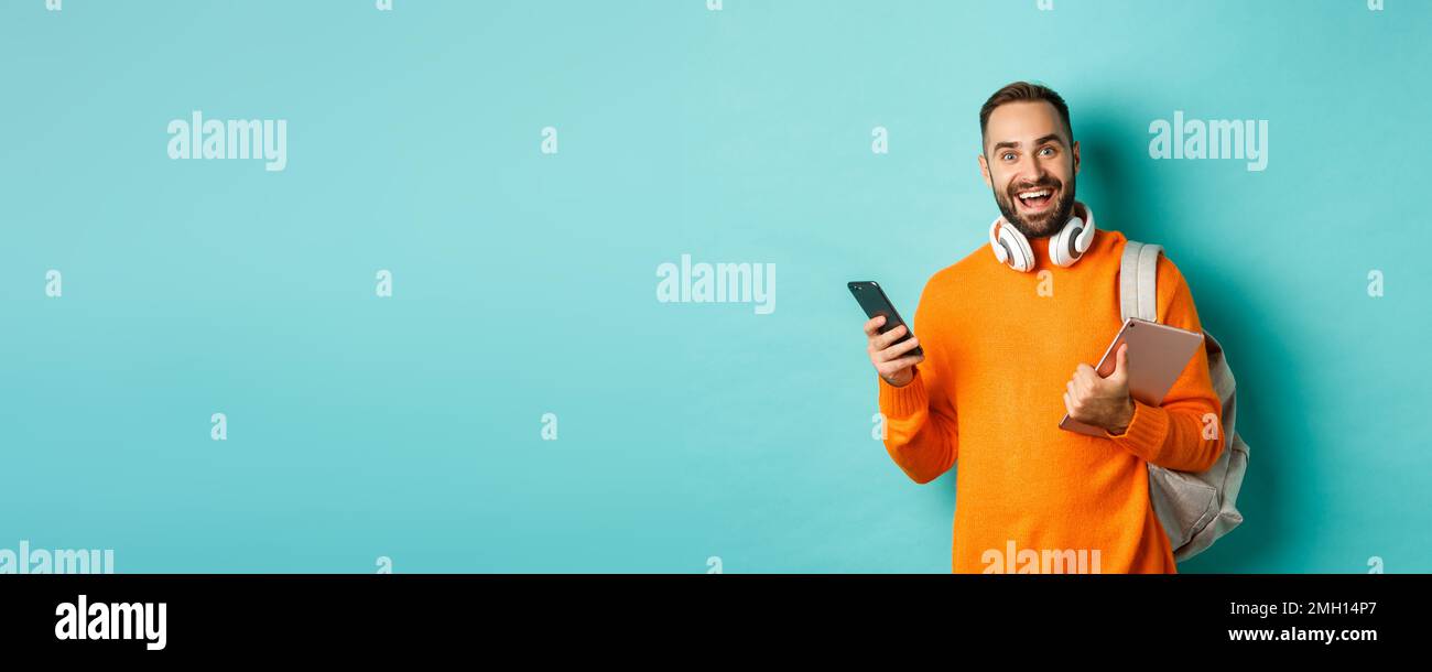 Handsome man student with headphones and backpack, holding digital ...