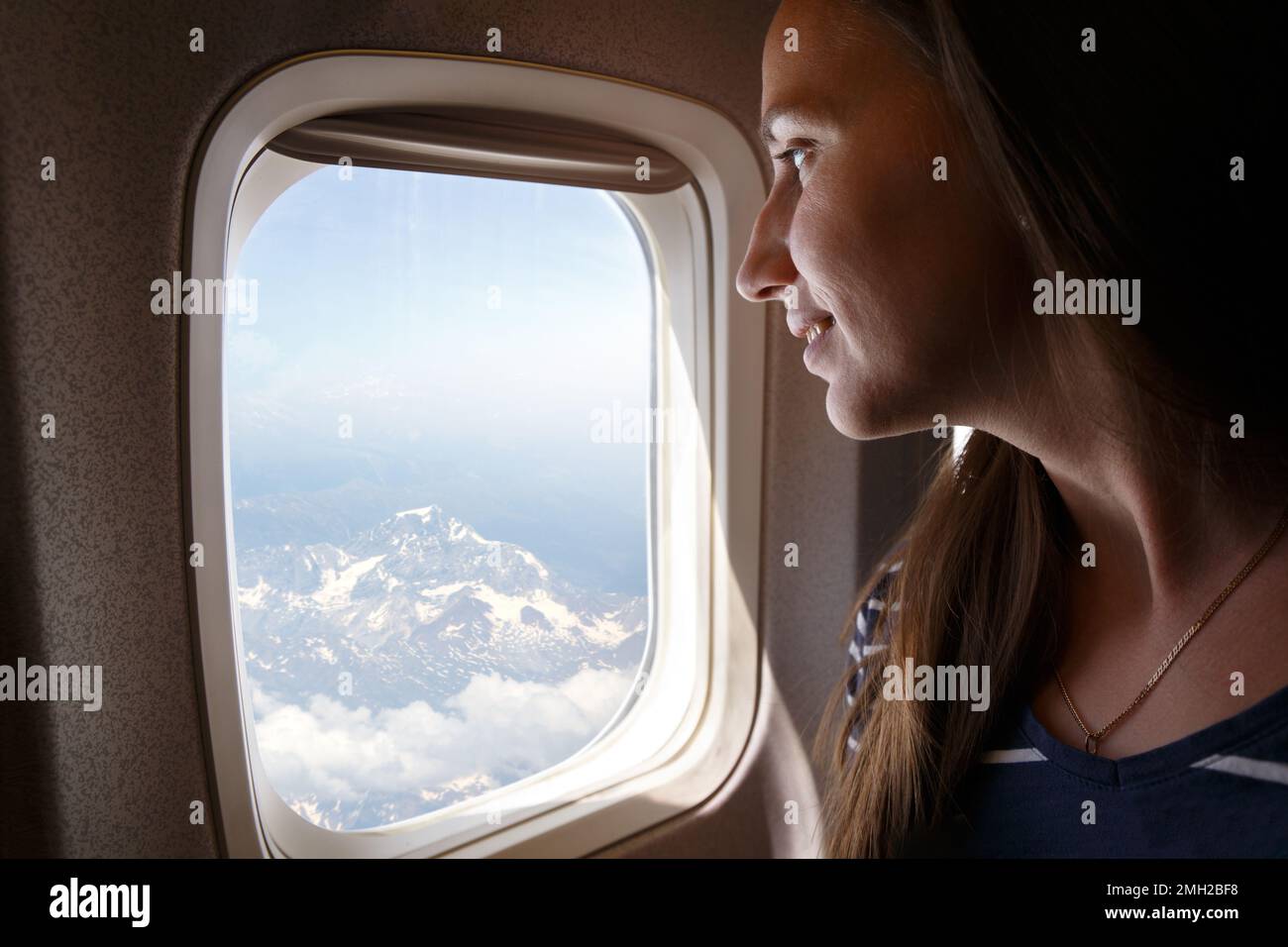 Young smiling woman looking through the plane window on the Alps ...