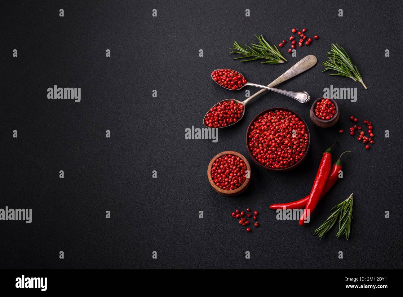 Spice, allspice peas in red or pink color in a wooden bowl on a black ...