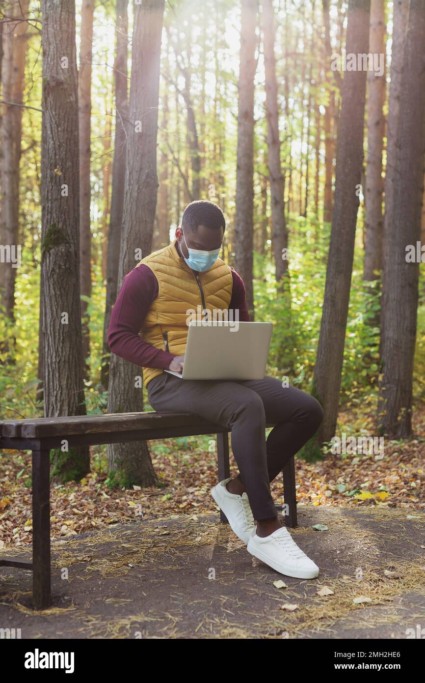 African american man in medical mask sitting in city park on a bench ...