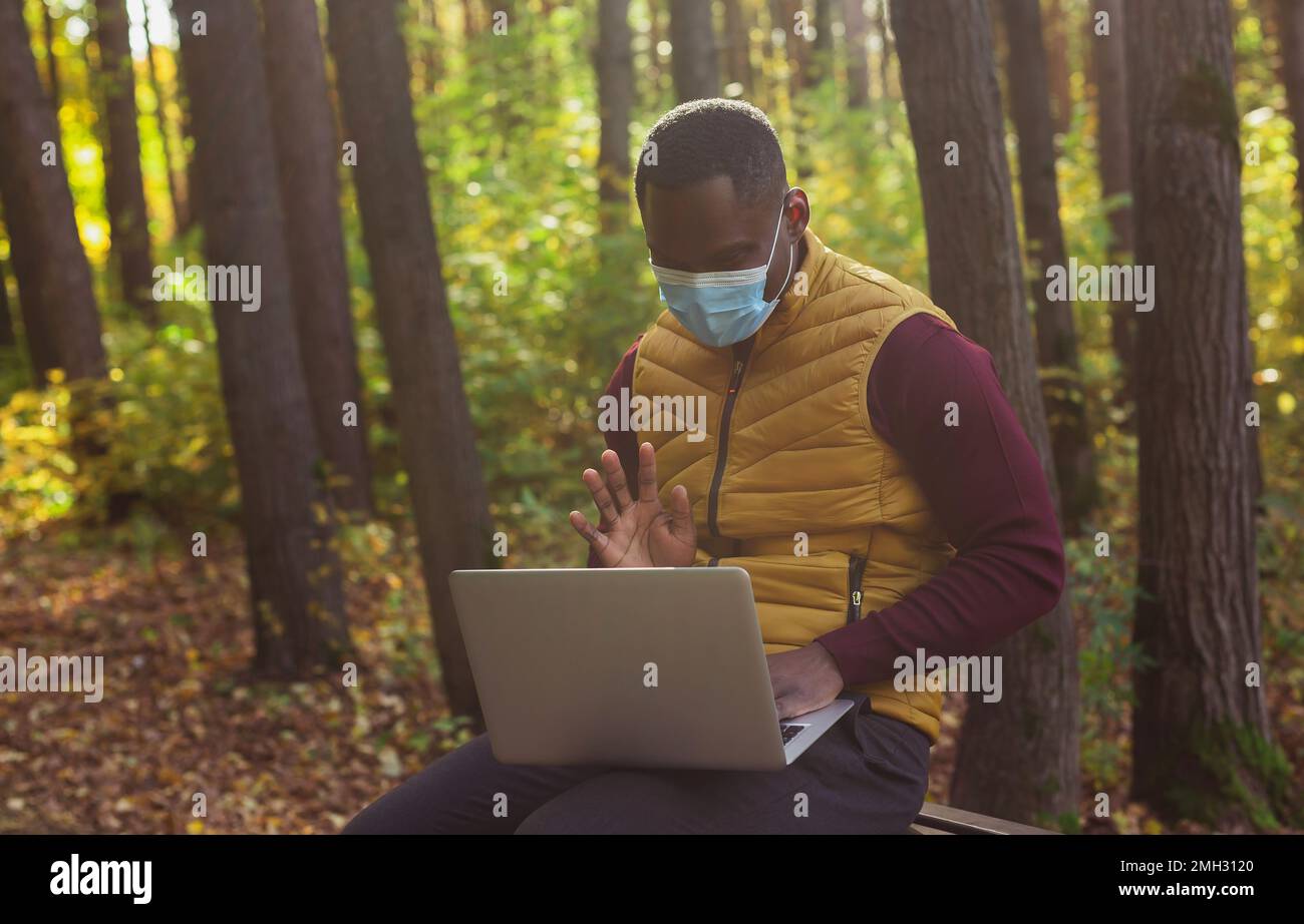 African american man in medical mask sitting in city park on a bench ...