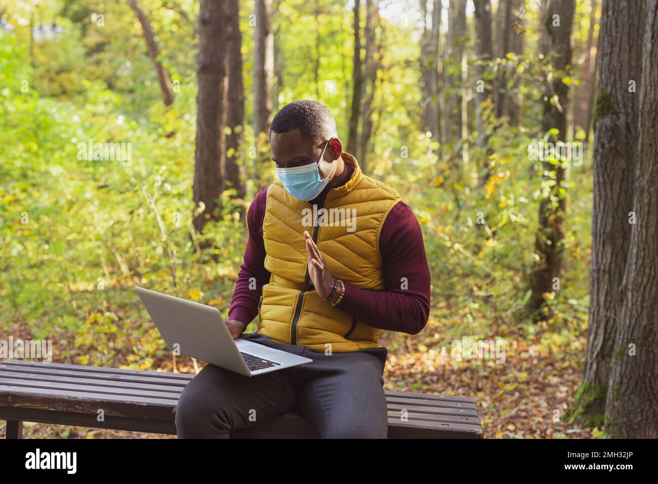 African american man in medical mask sitting in city park on a bench ...
