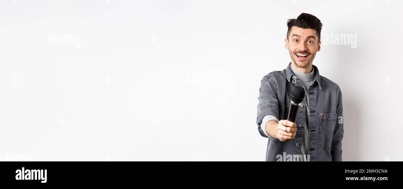 Handsome smiling man stretch out hand with microphone, giving you mic ...