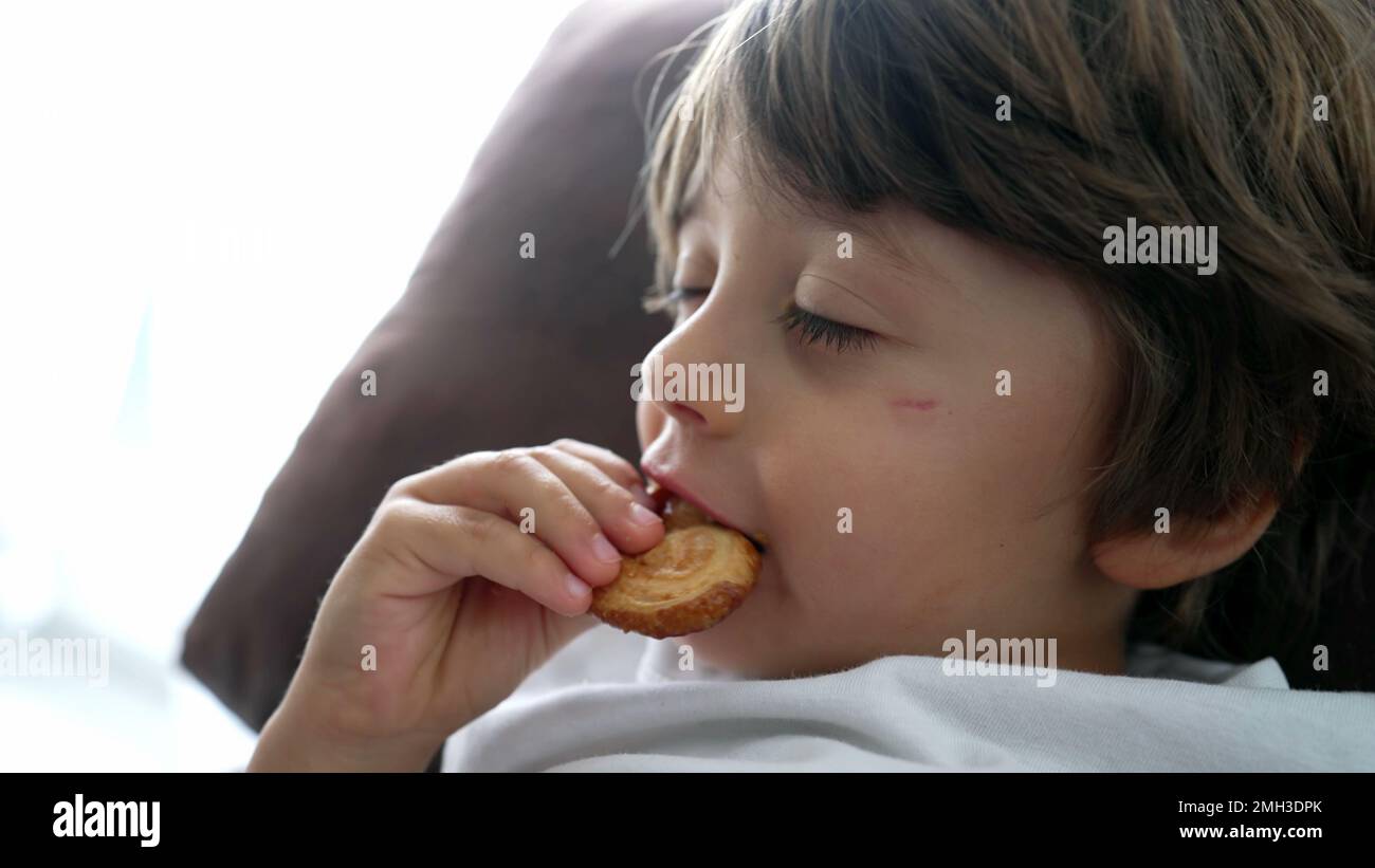 Close up child eating cookie laying on couch. Young boy eats snack ...