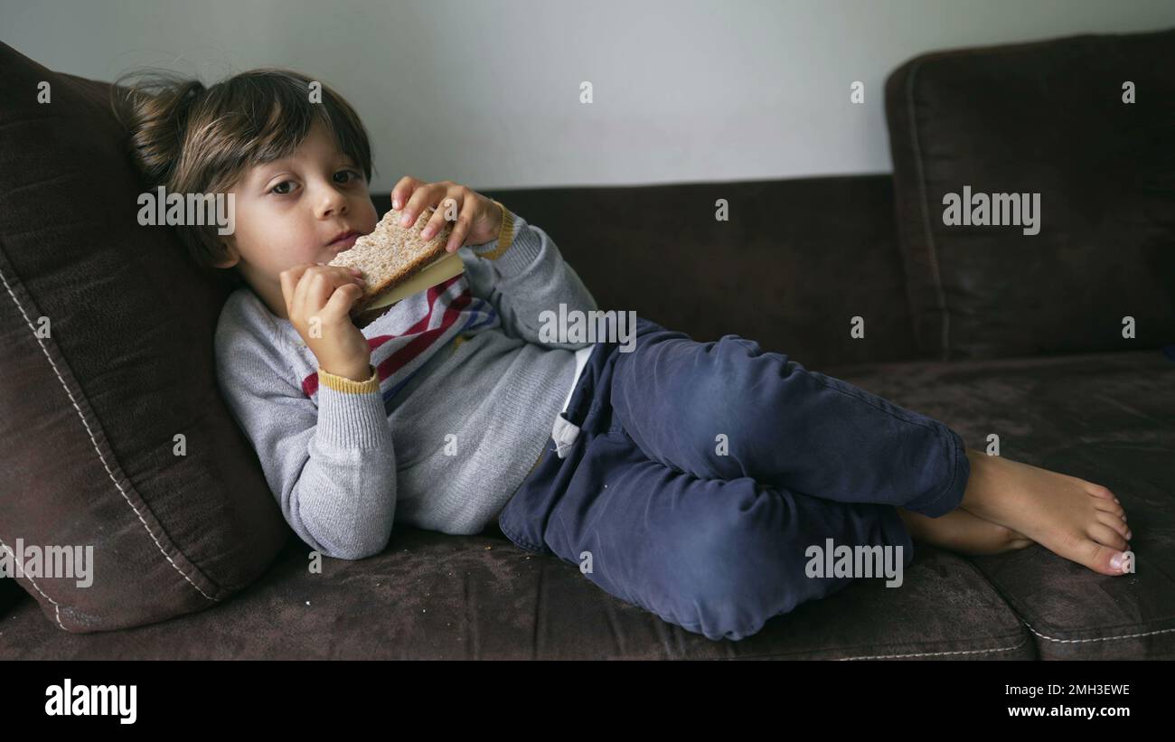 Child laying on couch snacking sandwich. Relaxed kid eating carb food ...