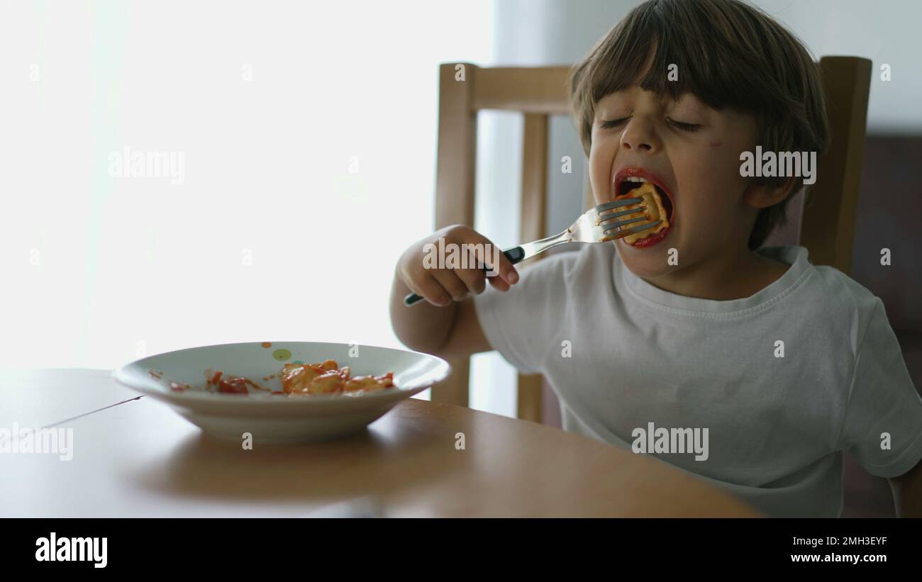 Child eating pasta ravioli by himself at home. One small boy eats carb ...