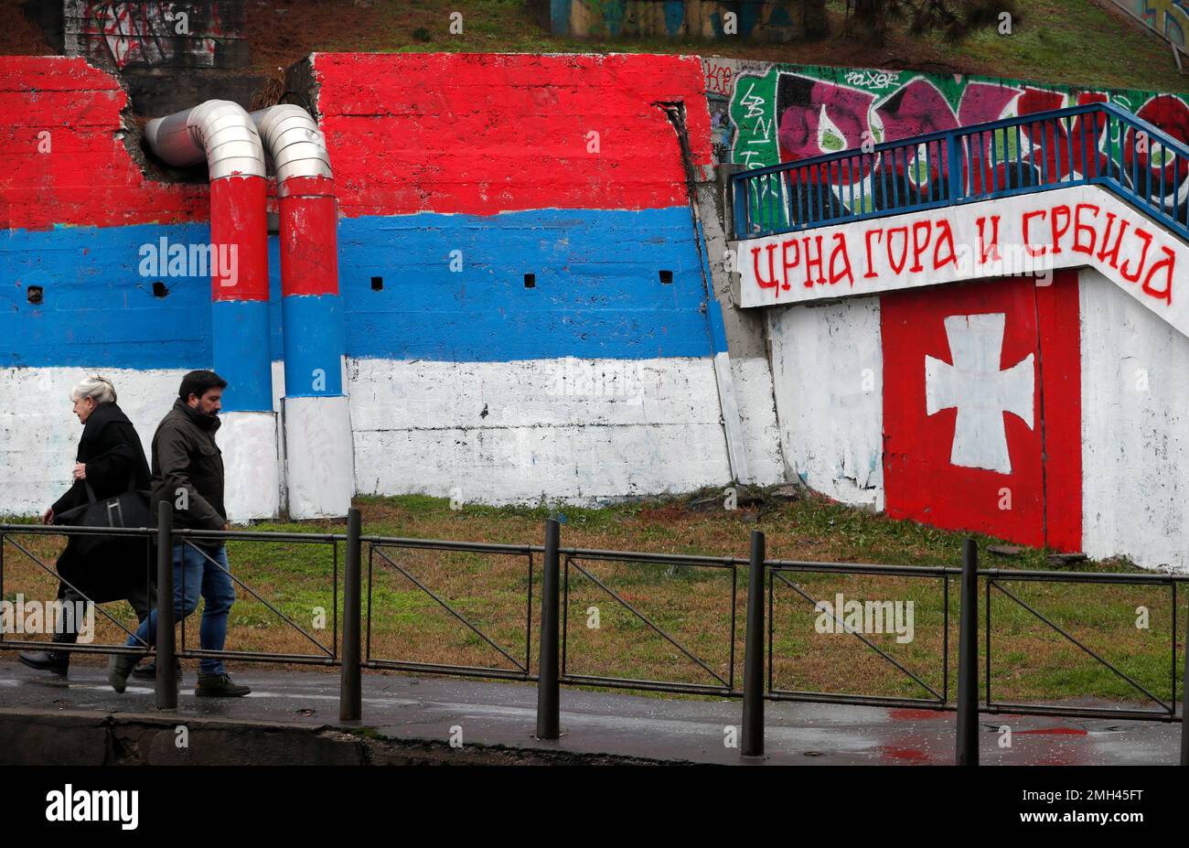 People walk by graffiti showing a Serbian flag, left, and text reading ...