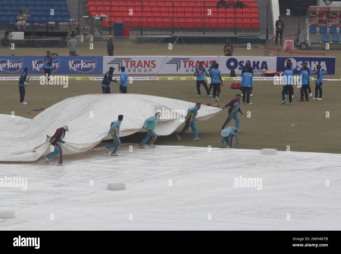 Ground staff cover a pitch during a light rain at Gaddafi stadium, in ...