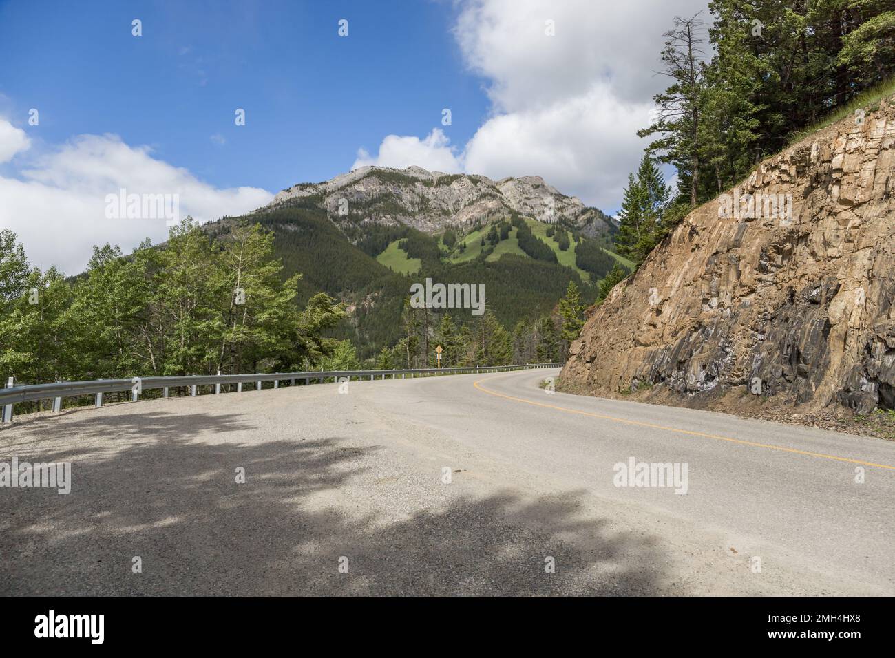 Curved empty country road passing through forest and green mountains in ...