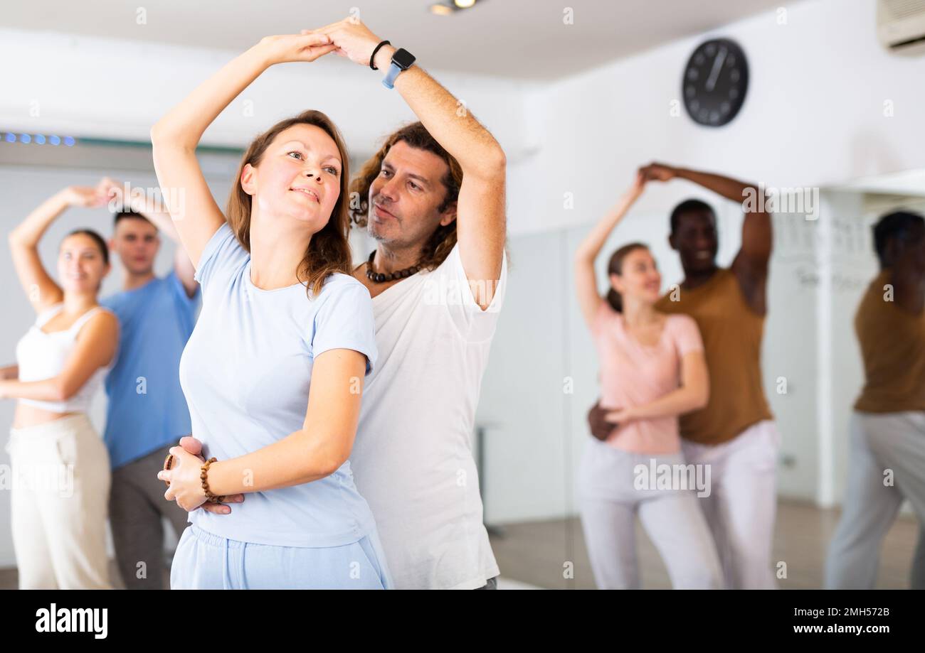 Positive smiling dancing couple enjoying active dancing during group ...